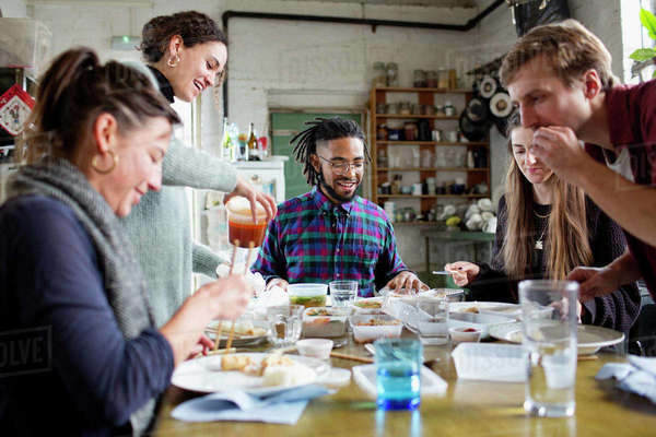 Young roommate friends enjoying takeout food at kitchen table in ...