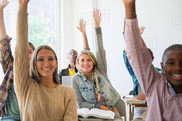 Teenage students raising hands in classroom - Stock Photo - Dissolve