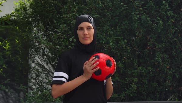 Beautiful female football player in hijab with ball in her hand. The woman plays soccer for ...