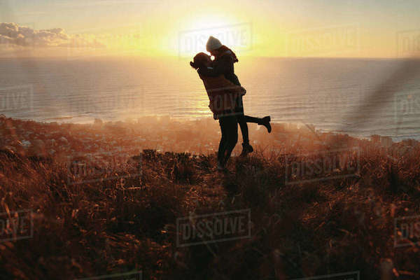 Silhouette of young man carrying his girlfriend on the mountain peak ...