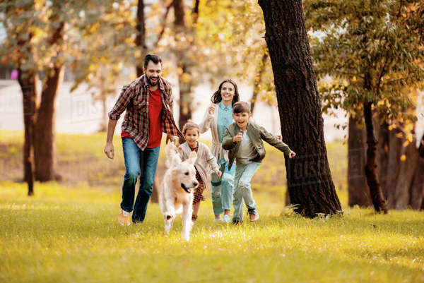 Happy family with two children running after a dog together in autumn ...