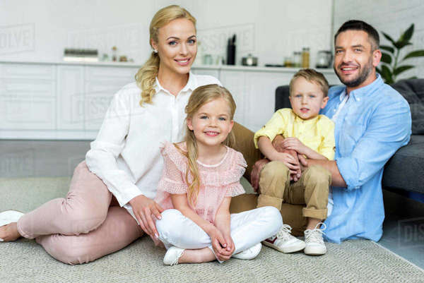 Happy family with two kids smiling at camera while sitting together at ...