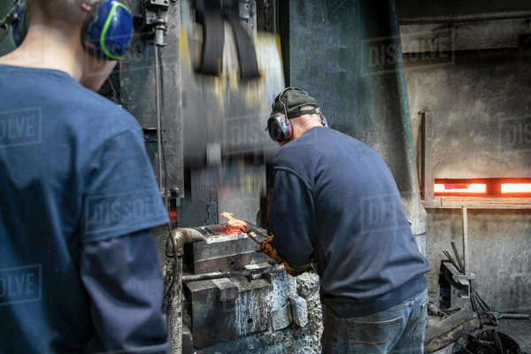 Engineer with apprentice forging steel parts in hammer press in industrial forge - Royalty-free ...