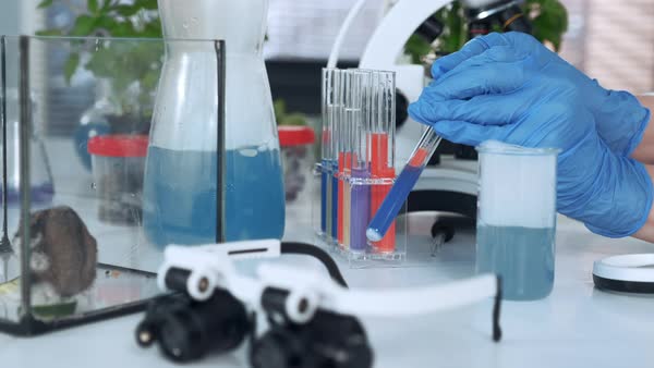 Close-up of scientist hands in lab gloves mixing compounds in test tube ...
