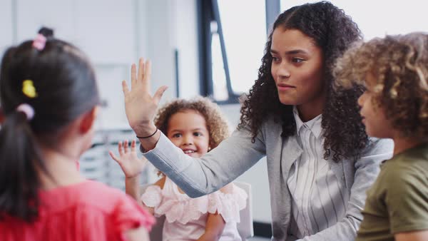 Infant school kids and teacher having a group high five in class after ...