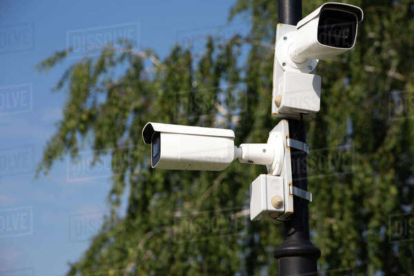 Two white surveillance cameras on a pole look in different directions ... Two white surveillance cameras on a pole look in different directions ...