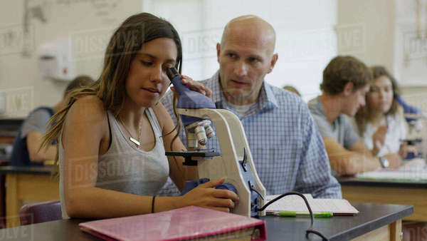 Teacher instructing student using microscope for scientific experiment ...