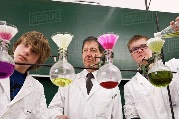 A teacher supervising two students conducting a chemistry experiment ...