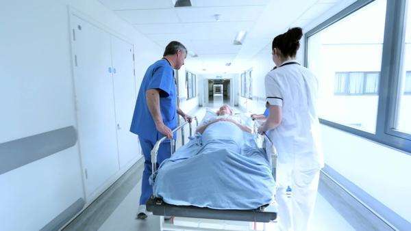 Caring Caucasian medical staff moving patient on hospital bed through ...