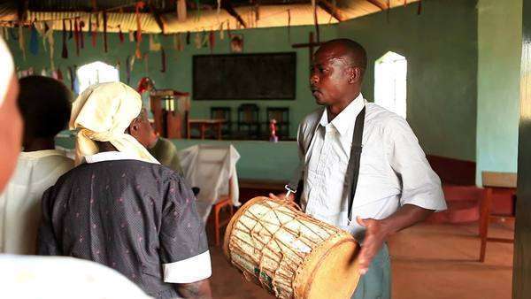 Close up of a male drummer singing next to worshipers in a Kenyan ...