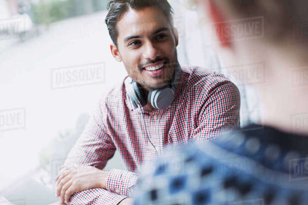 Smiling young man with headphones talking to window at cafe window ...