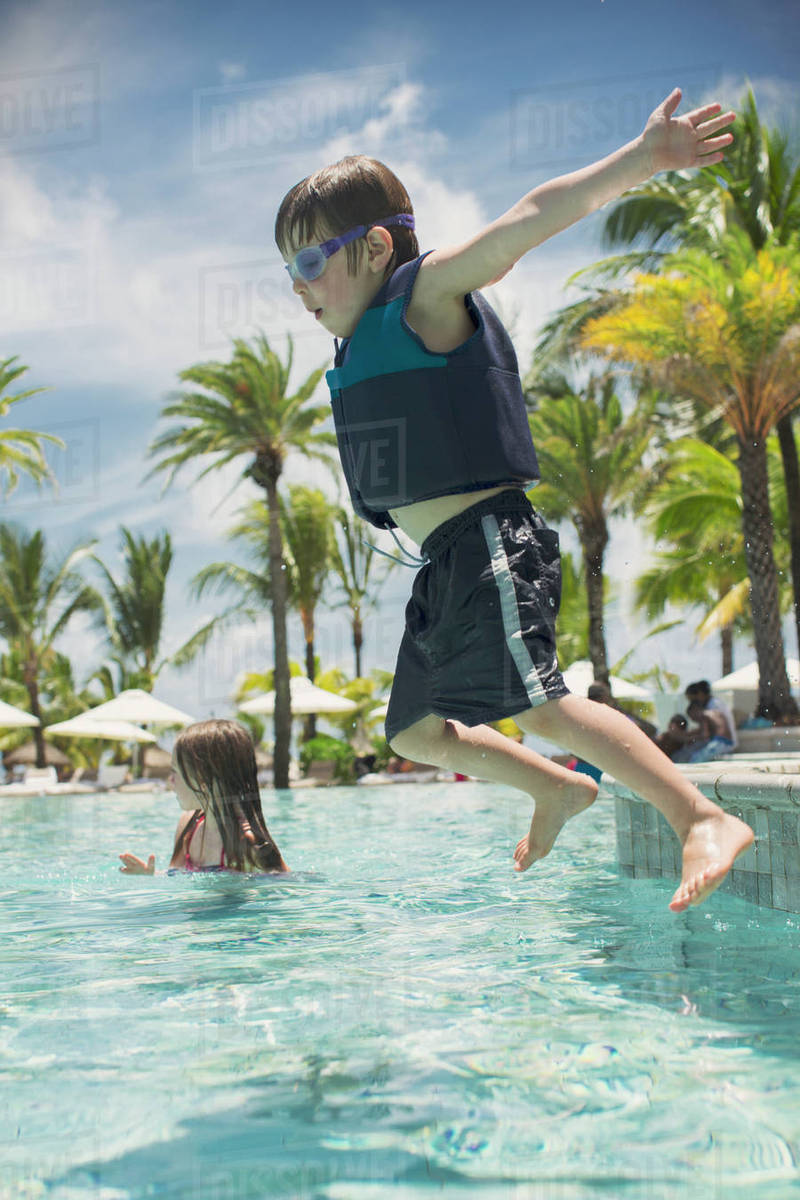 Boy jumping into sunny tropical swimming pool - Stock Photo - Dissolve