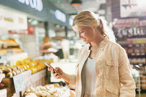 Young woman using cell phone in grocery store market - Royalty-free ...