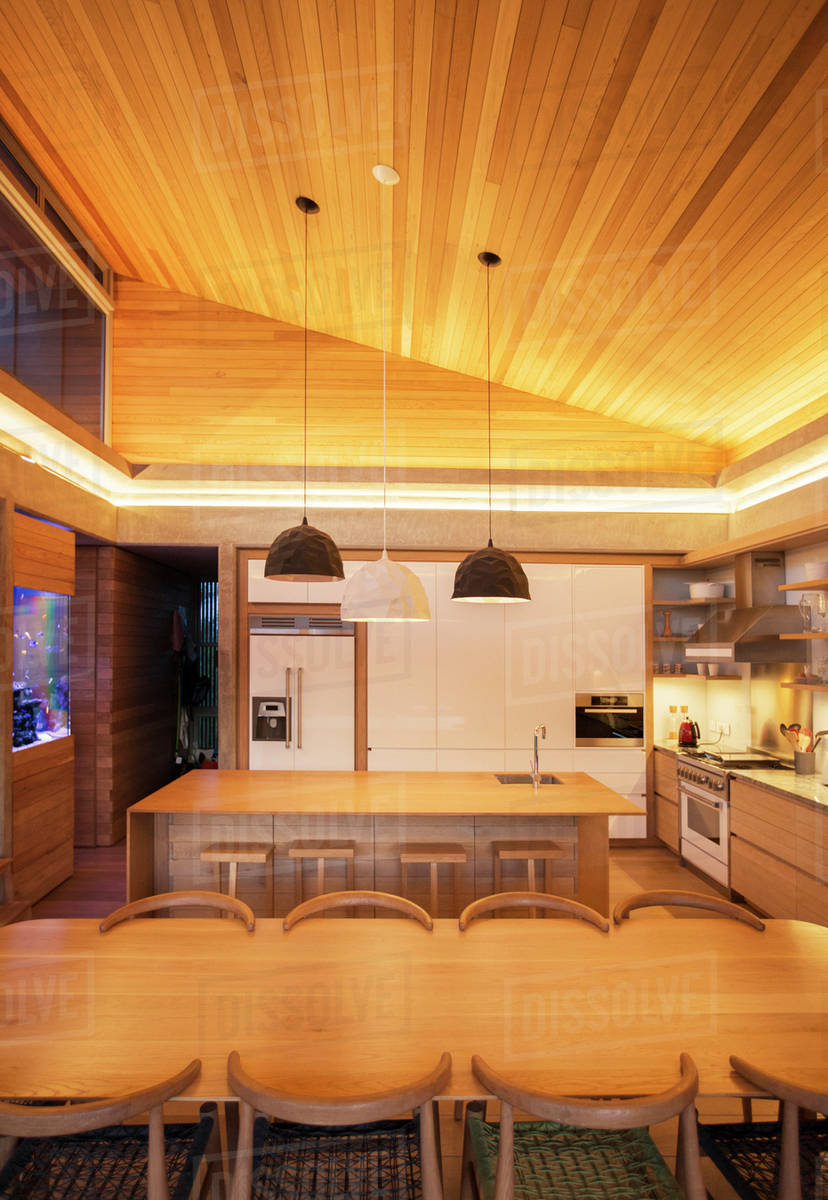 Illuminated slanted wood ceiling over luxury kitchen and dining table ...