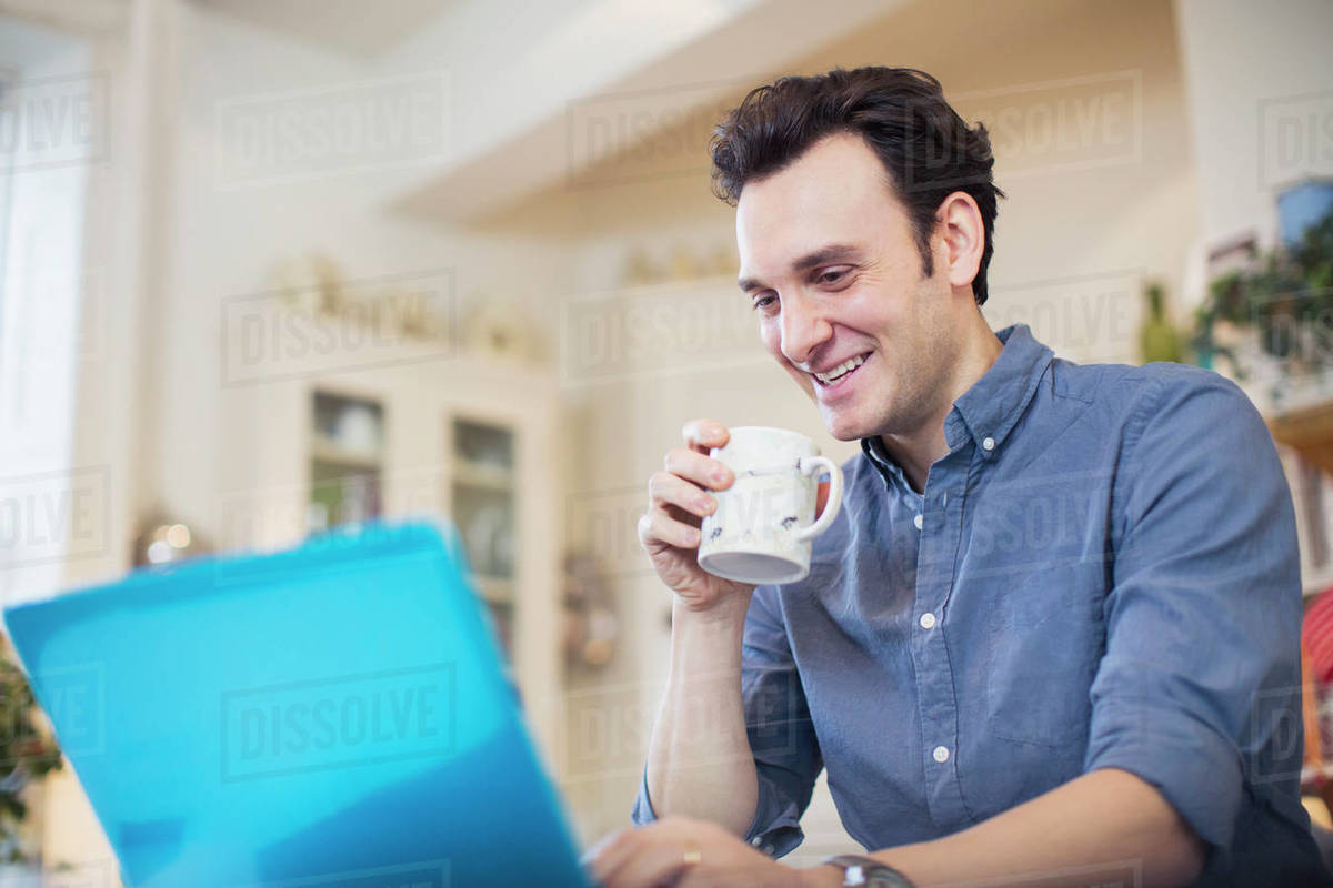 Smiling man drinking coffee, working at laptop - Royalty-free Stock ...