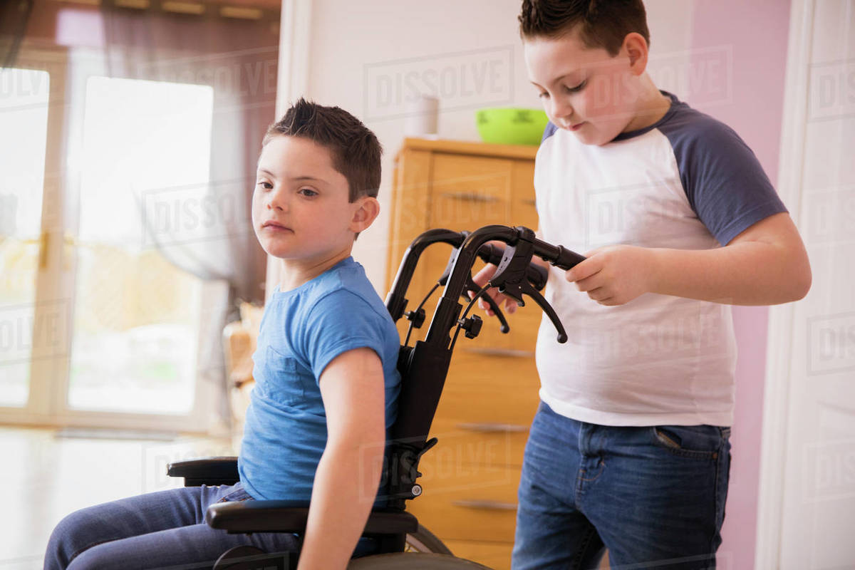 Boy pushing brother with Down Syndrome in wheelchair - Royalty-free ...
