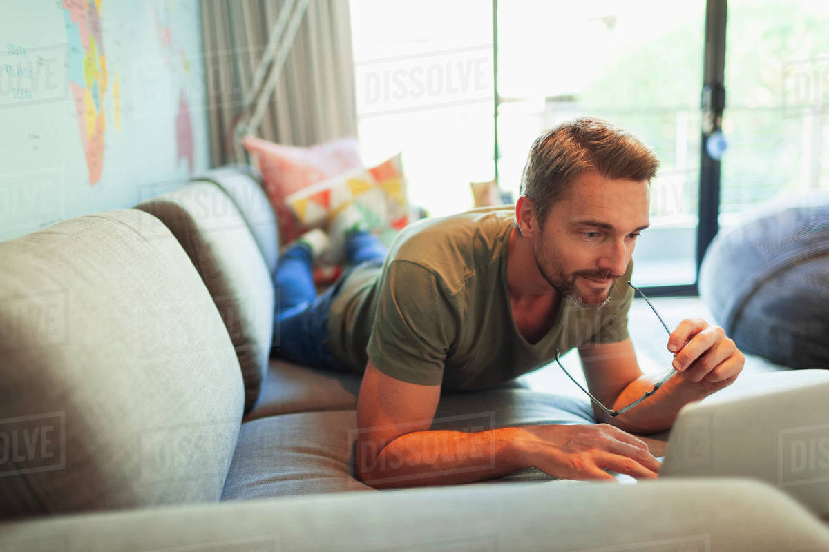 Man relaxing, laying on sofa using laptop - Royalty-free Stock Photo ...