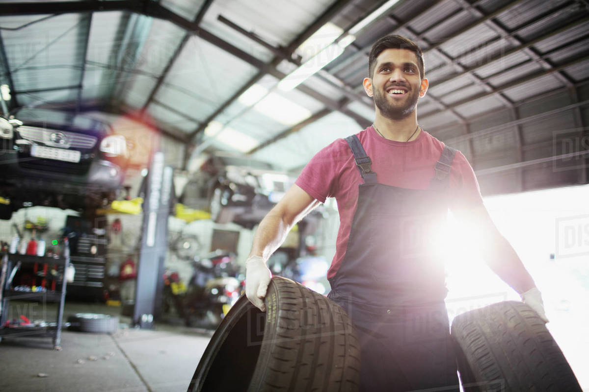 Portrait smiling male mechanic carrying tires in auto repair shop ...