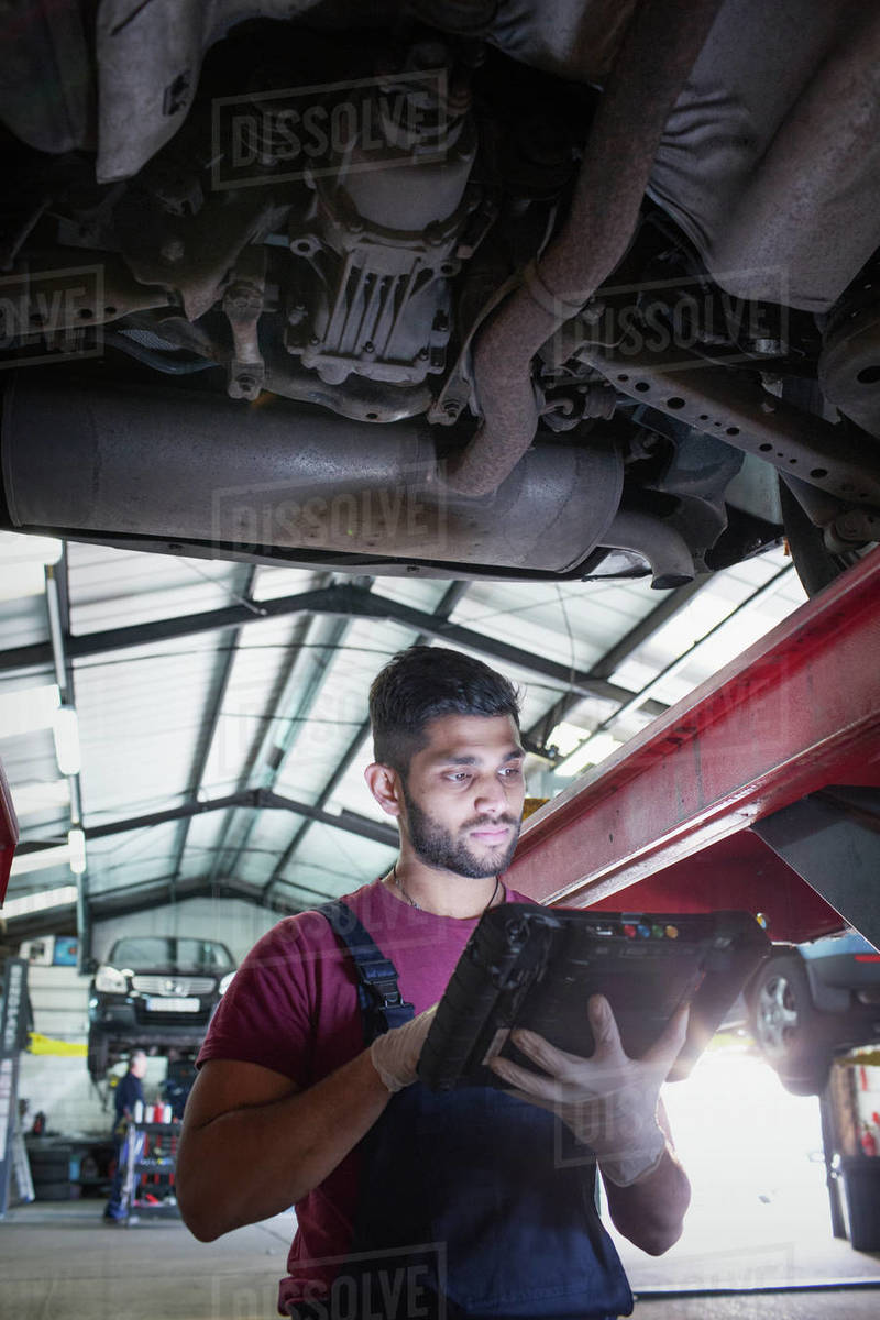 Male mechanic using diagnostic equipment under car in auto repair shop ...