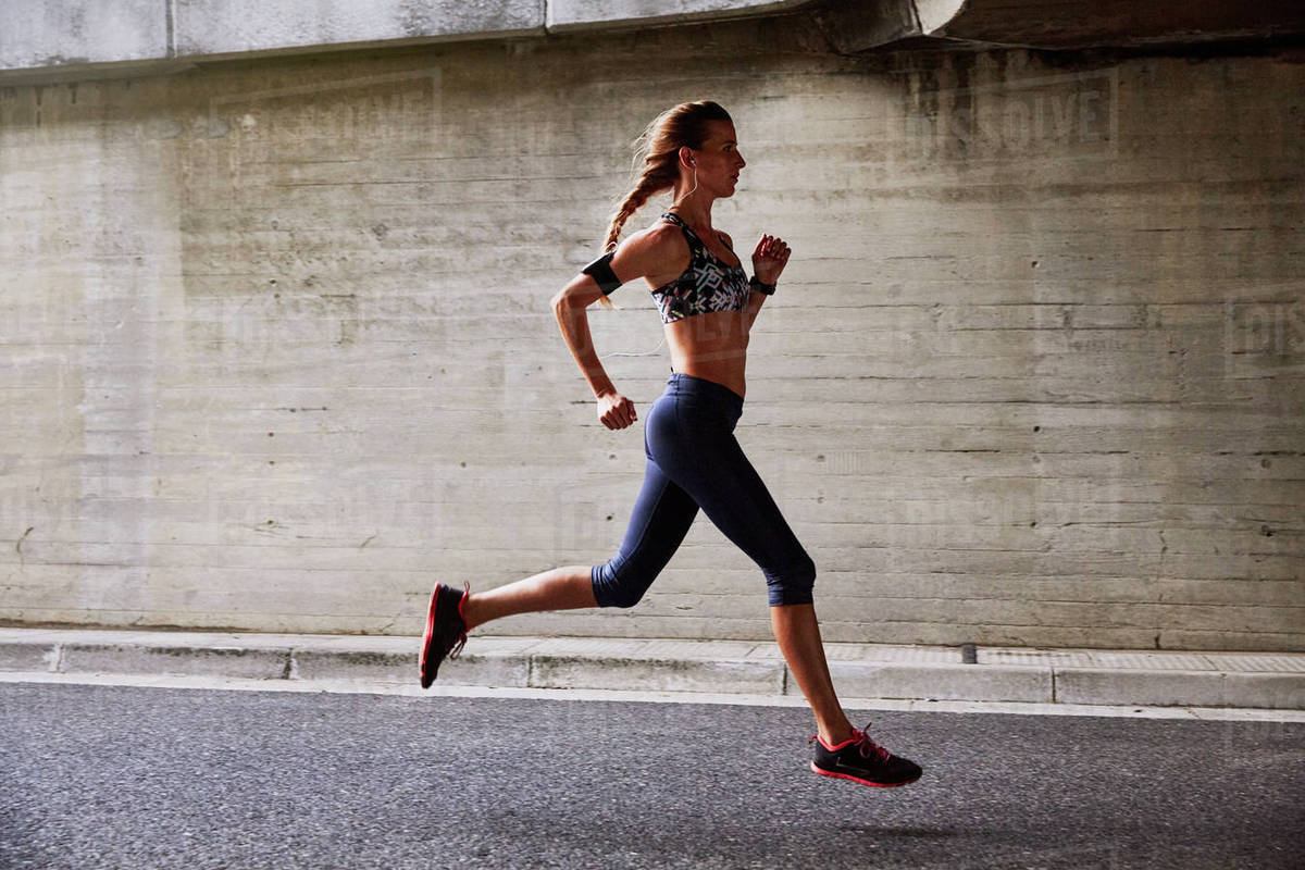 Female runner running on urban street - Royalty-free Stock Photo | Dissolve