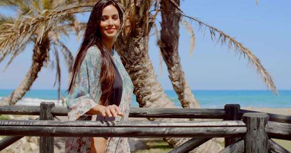 Smiling pretty young woman in summer beach wear standing at the wooden ...