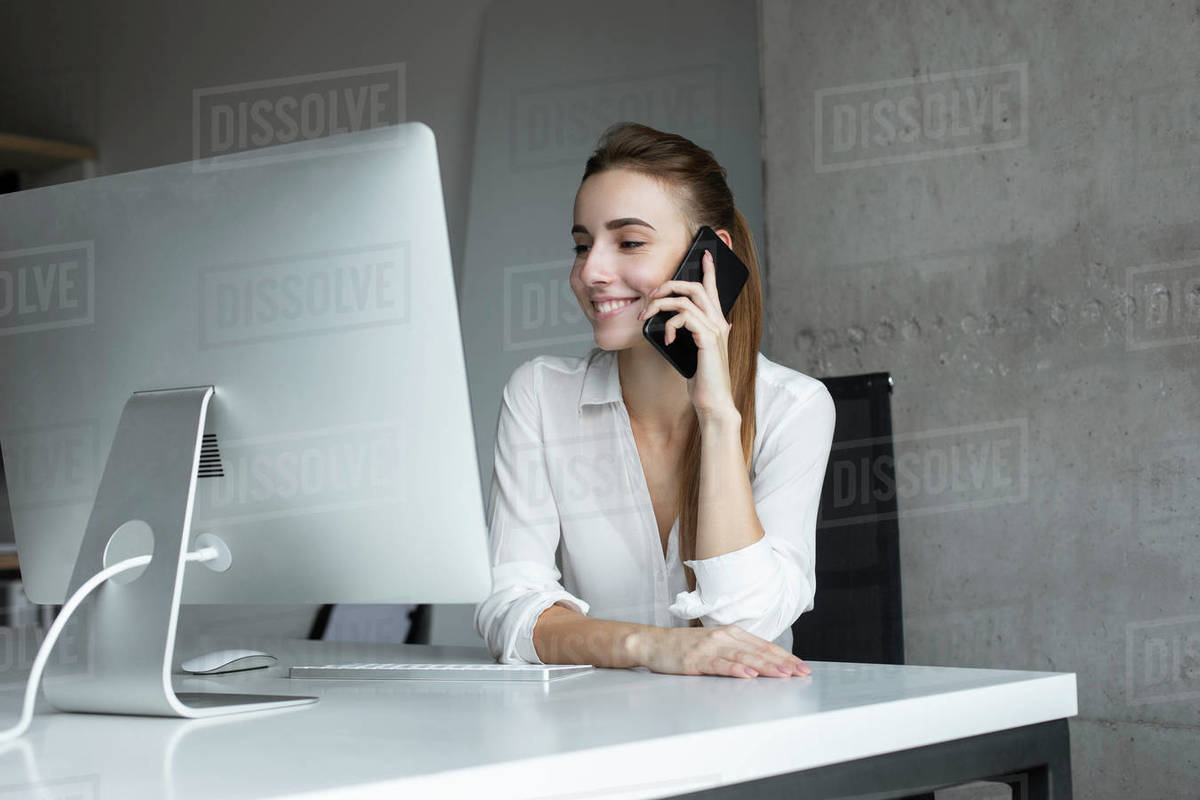 Smiling businesswoman taking phone call at desk - Stock Photo - Dissolve