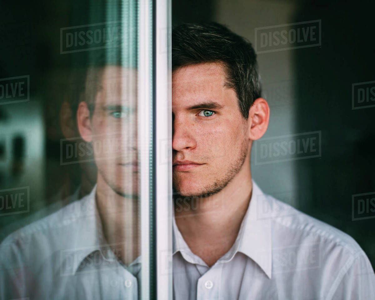 Portrait of man looking around glass door - Stock Photo - Dissolve