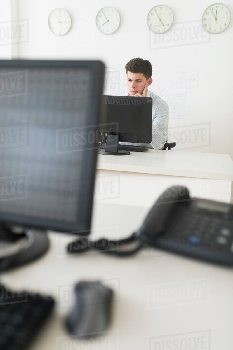 Young man sitting in front of desk and working - Stock Photo - Dissolve