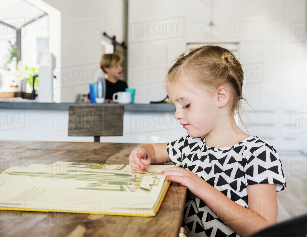 Girl reading picture book at dining table - Stock Photo - Dissolve