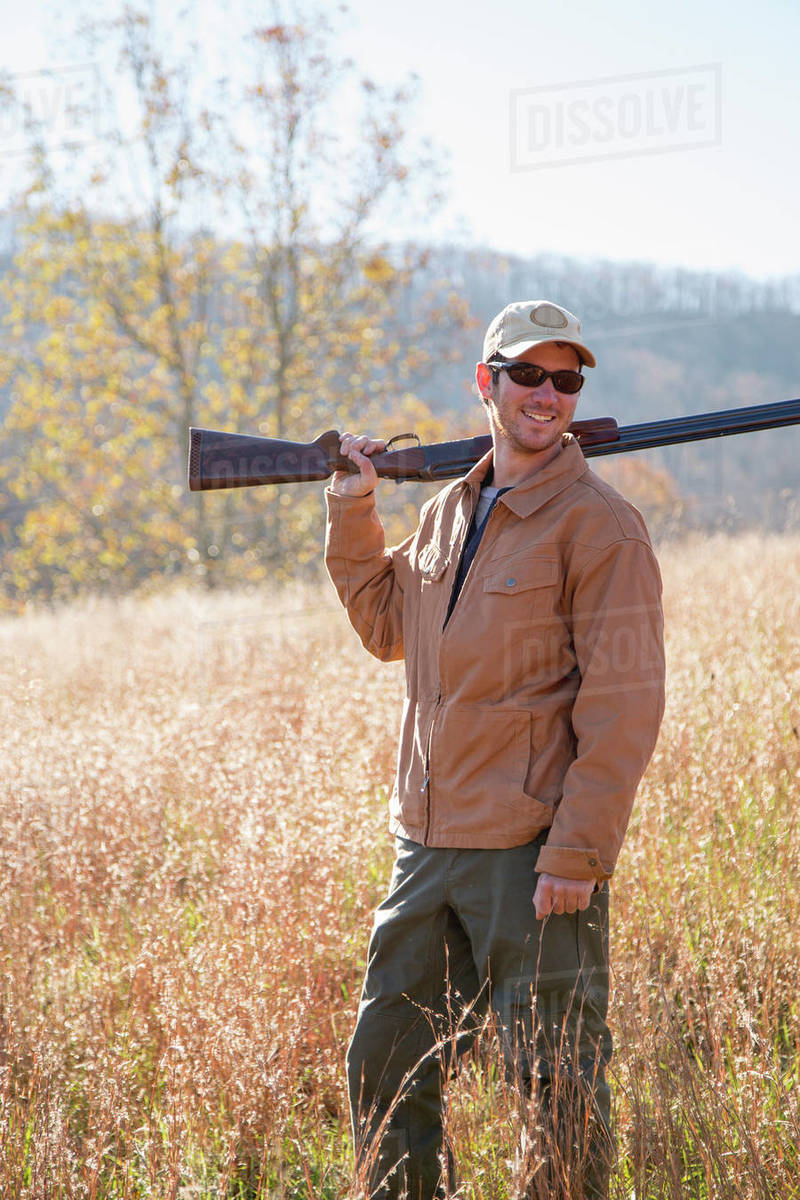 Smiling young man holding rifle in field - Royalty-free Stock Photo ...
