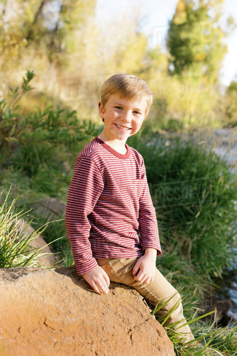 Smiling boy sitting on rock - Stock Photo - Dissolve