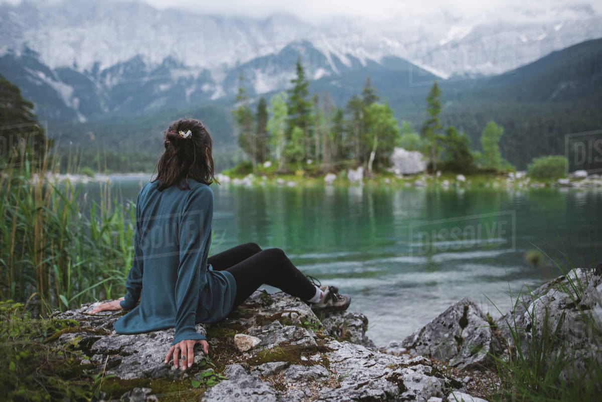 Germany, Bavaria, Eibsee, Young woman sitting on rock at shore of ...