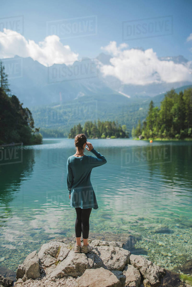 Germany, Bavaria, Eibsee, Young woman standing on rock at shore of ...