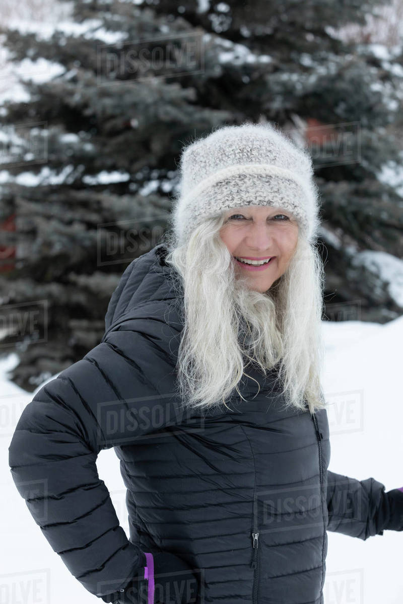 Smiling woman wearing hat and jacket in snow - Stock Photo - Dissolve