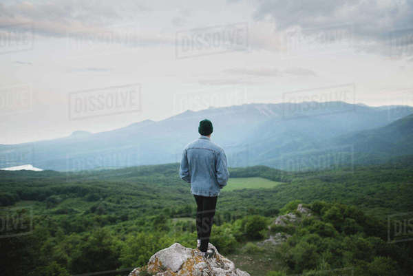 Man standing on cliff by mountain and forest - Stock Photo - Dissolve
