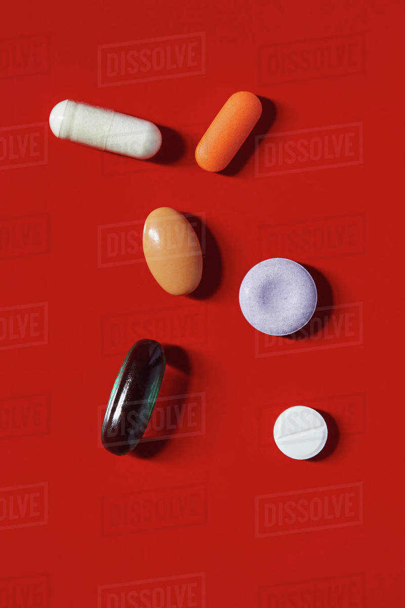 Various pills and capsules on red background - Stock Photo - Dissolve