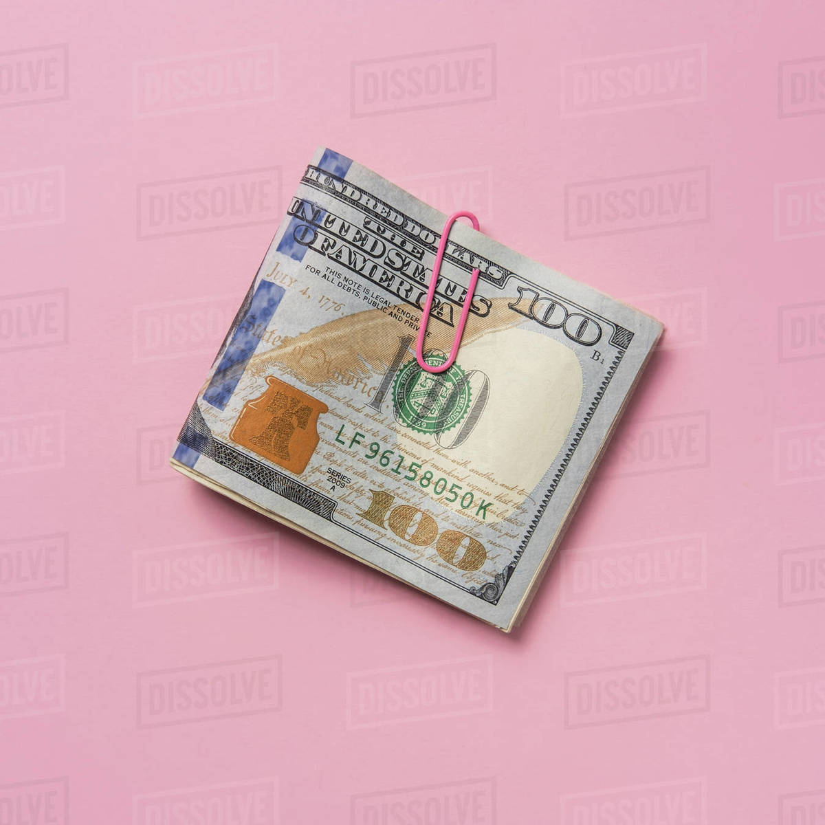 Folded one hundred dollar bill with paper clip on pink background ...