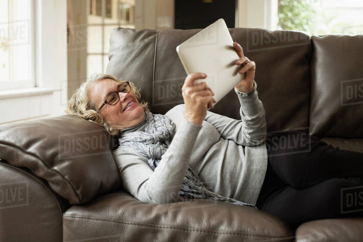 Senior woman reclining on sofa looking at digital tablet - Royalty-free ...