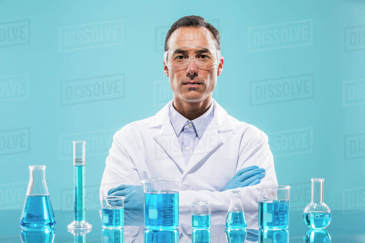 Portrait of scientist with beakers with blue liquid in foreground ...