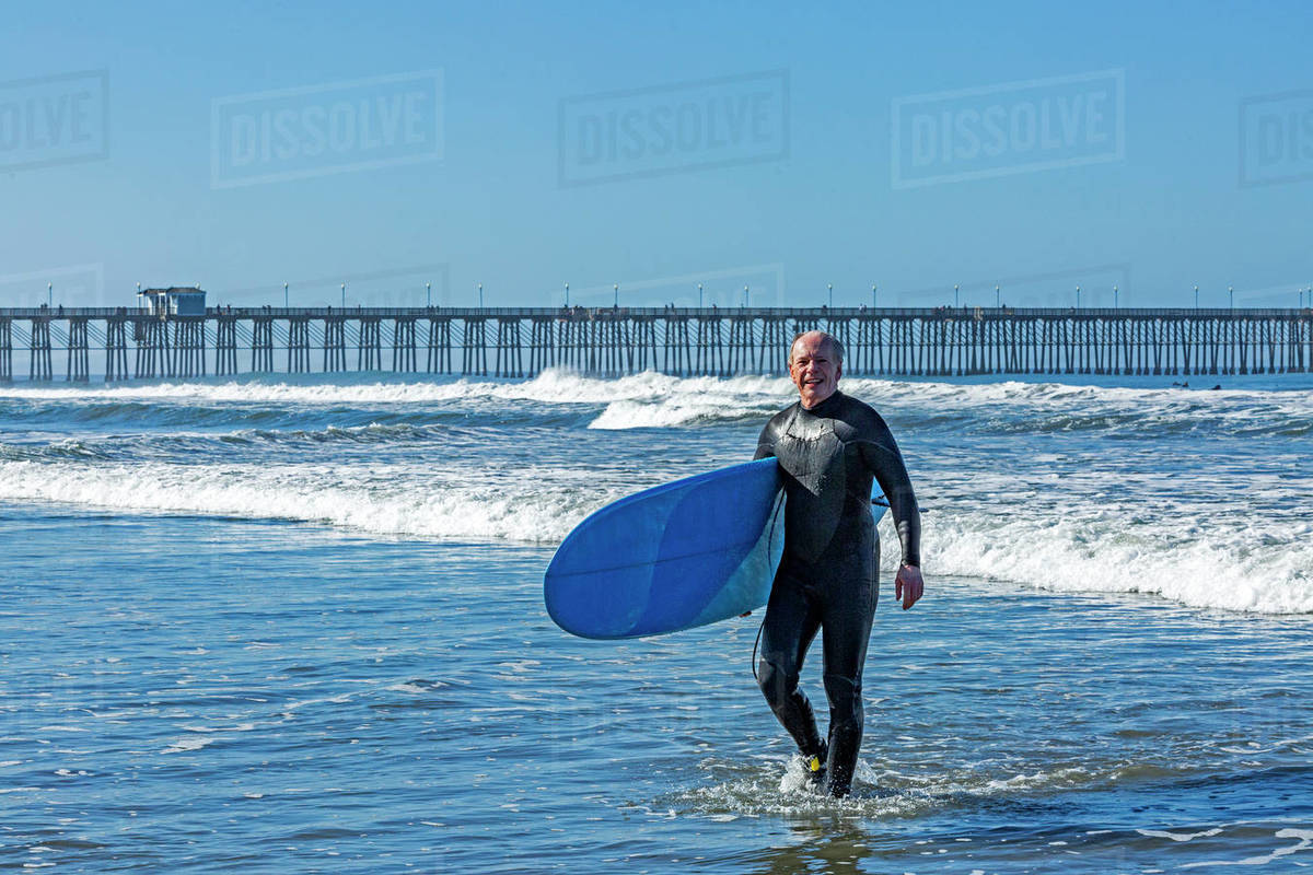 USA, California, Oceanside, Senior surfer carrying surfboard - Royalty ...