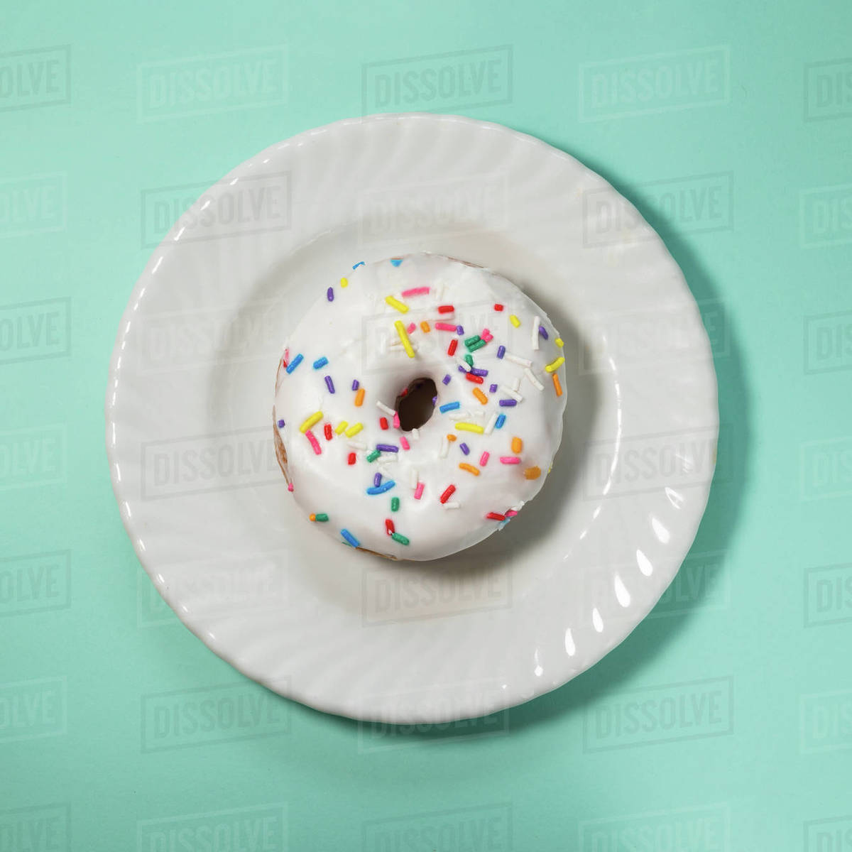Overhead view of donut with white icing and sprinkles on white plate ...