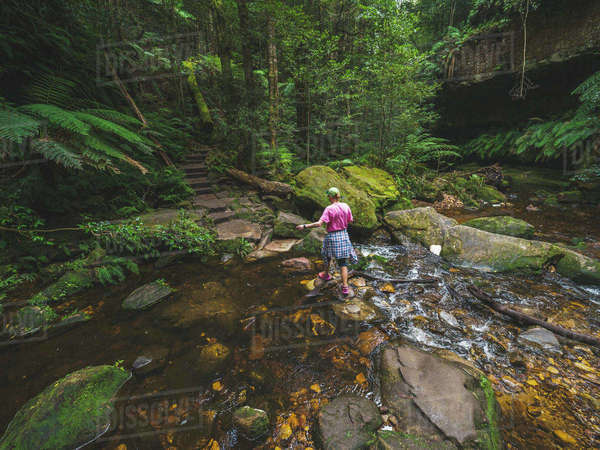 Rear view of woman crossing shallow stream in forest - Royalty-free ...