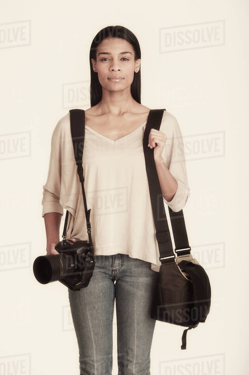 Studio portrait of woman carrying camera with bag - Stock Photo - Dissolve