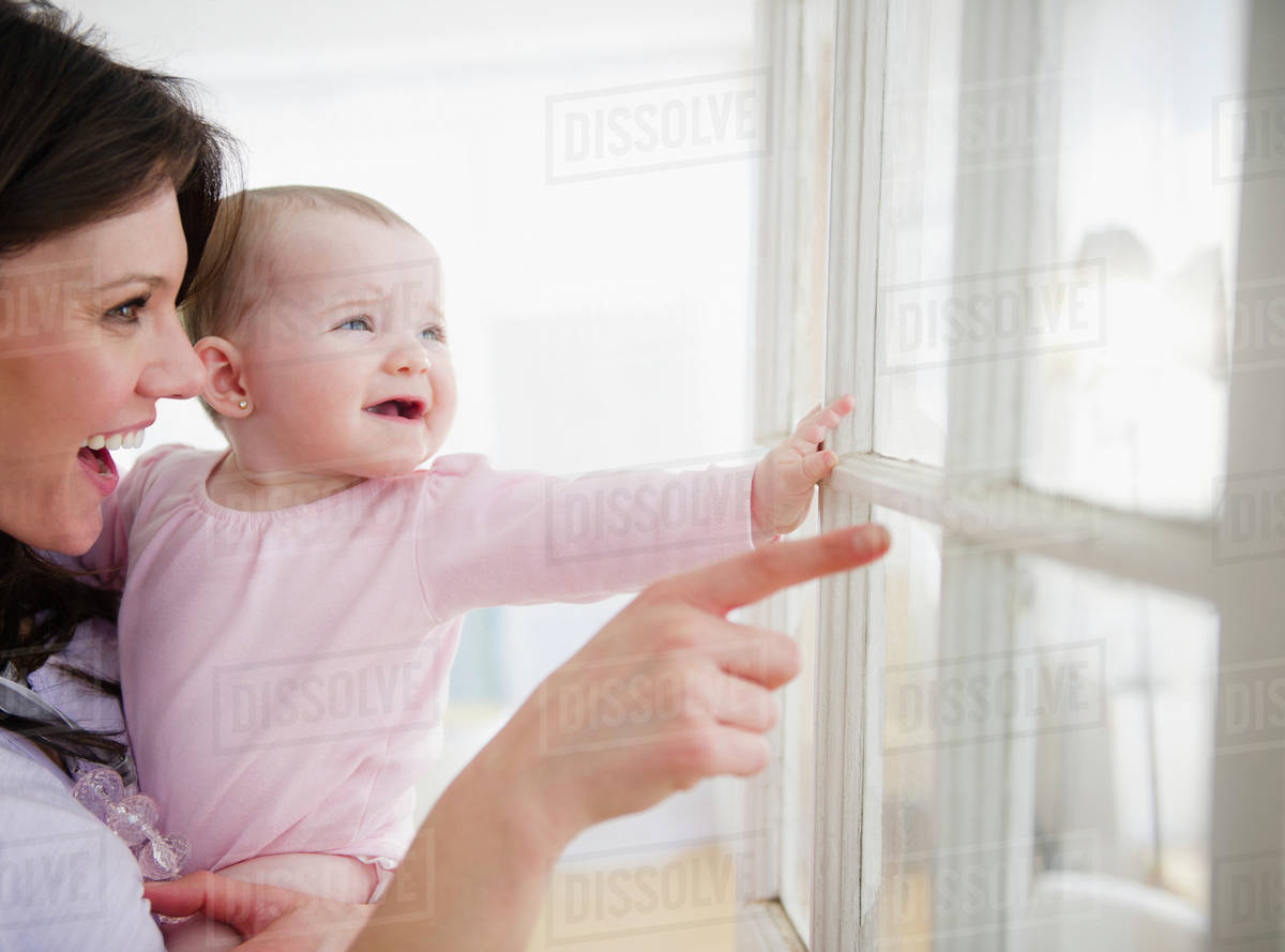 Mother with baby daughter (6-11 months) looking through window ...