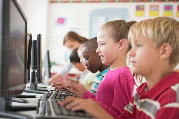 School children (8-9) with female teacher working with computers ...