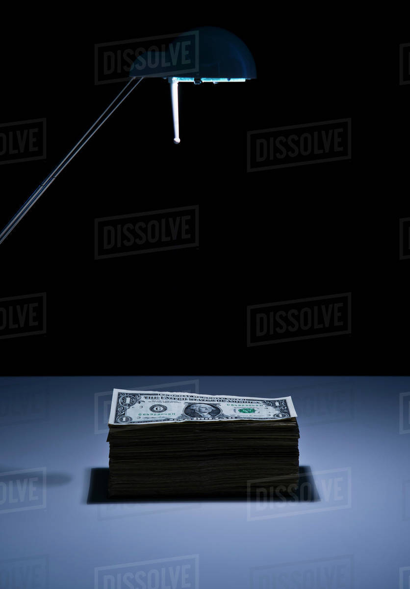 Stack of dollars under desk lamp - Royalty-free Stock Photo | Dissolve