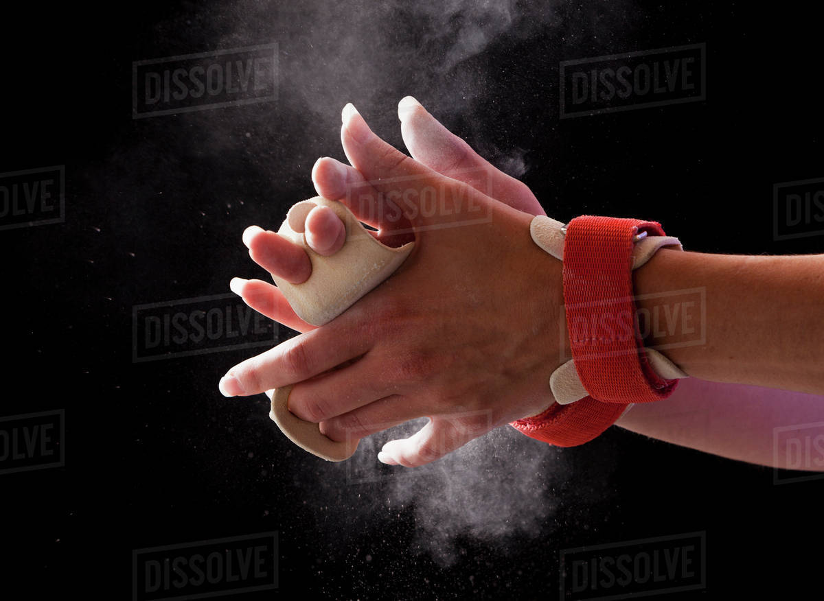 Close-up of gymnast's hands with chalk floating in air around them ...