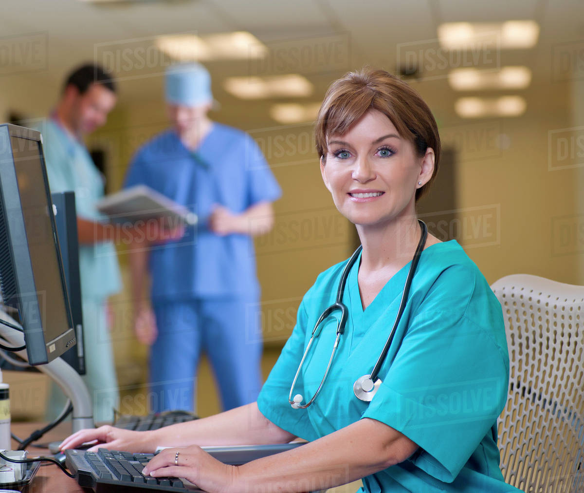 Female surgeon working on computer in hospital, colleagues in ...