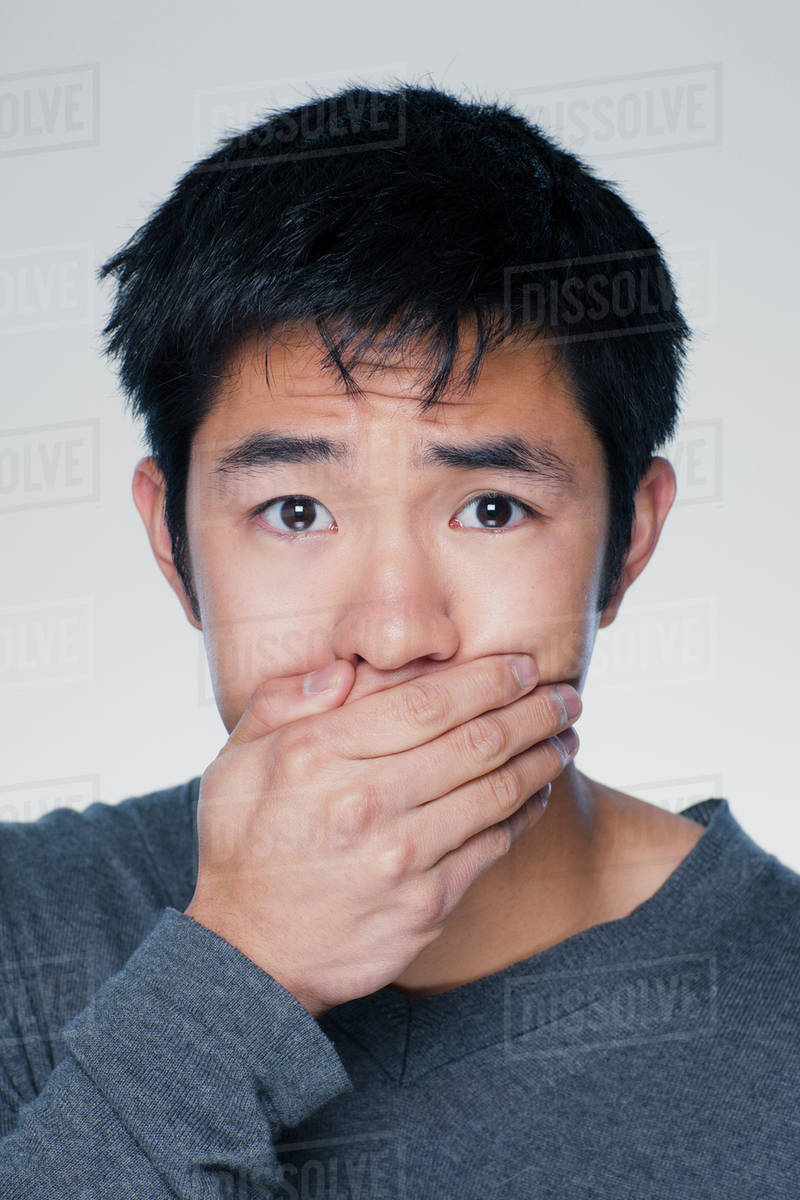 Studio portrait of young man covering mouth - Stock Photo - Dissolve