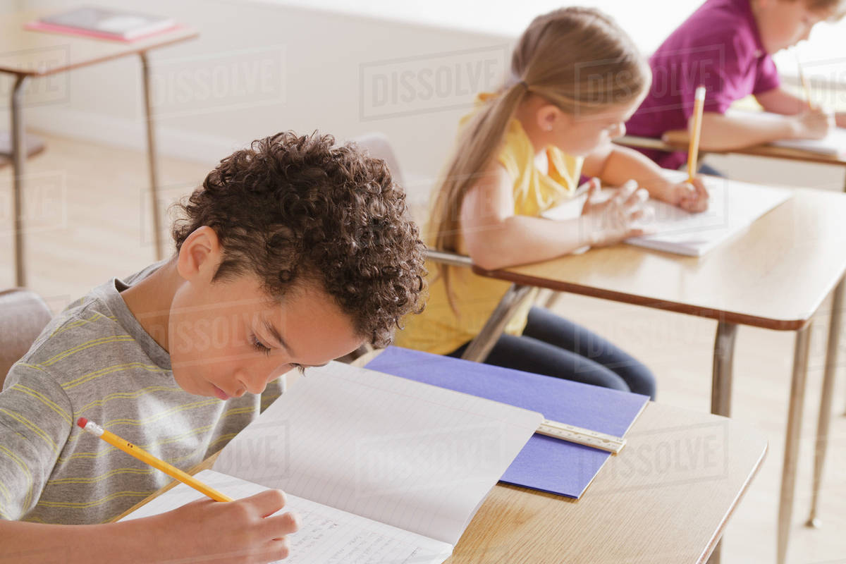 Schoolchildren focused on writing in classroom - Stock Photo - Dissolve